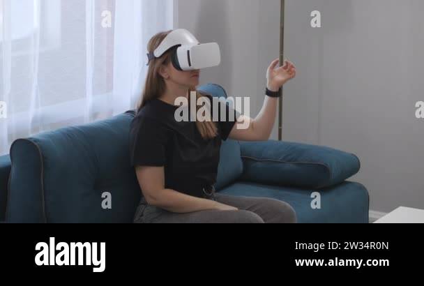 female user is using HMD-display for viewing interior of modern flat, sitting on couch in living ...