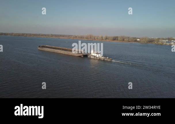 A tugboat ship pushes a barge upstream of the river to transport bulk ...