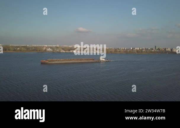 A tugboat ship pushes a barge upstream of the river to transport bulk ...