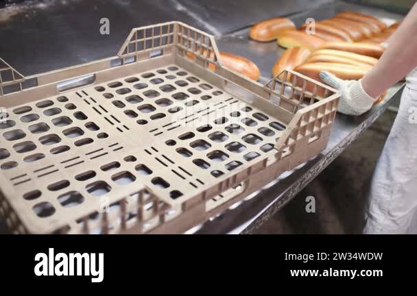 young Baker takes fresh loaves and pastries from a production line or ...