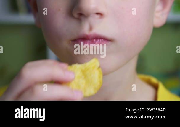 Smiling boy enjoys chips. Young caucasian kid eating unhealthy potatoes ...