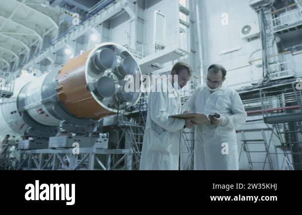 Two scientist engineers inspect the spacecraft, write on the tablet. A ...