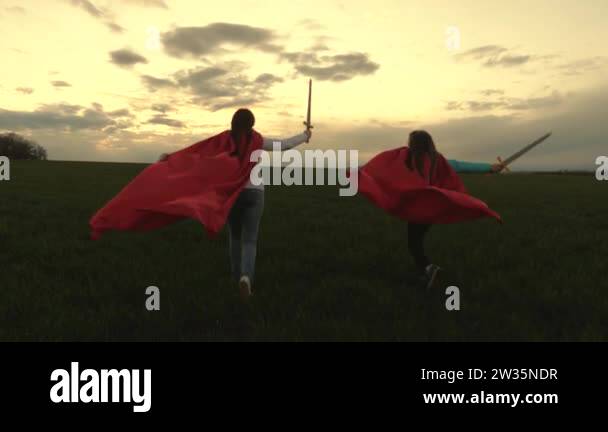 girls in red cloaks run with swords in hand across field playing ...