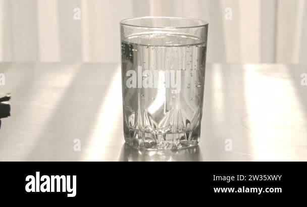 Dropping of soluble pill into glass of transparent water. Medication ...