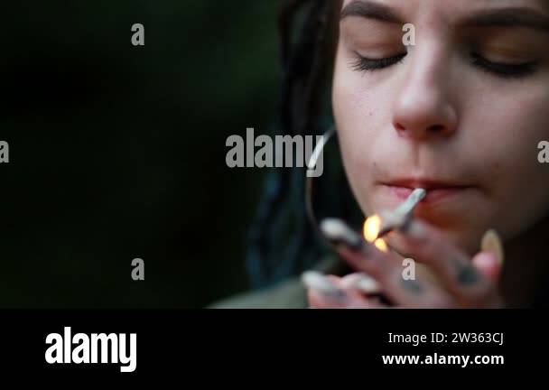 Woman Smoking Cannabis at Sunset, Close Up. The woman rolled the joint from fresh marijuana weed ...