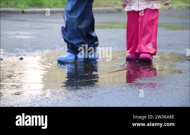Happy children jumping in puddle in waterproof coat. Boy and girl have ...