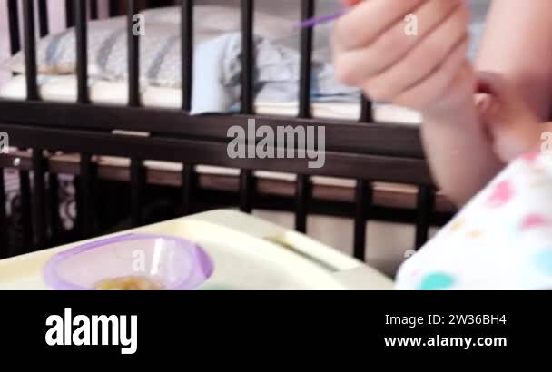 mother holds the baby in her arms and feeds her boy with a spoon ...