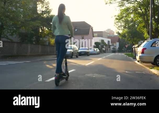 LENS FLARE: Young woman rides an electric scooter down an empty road in ...