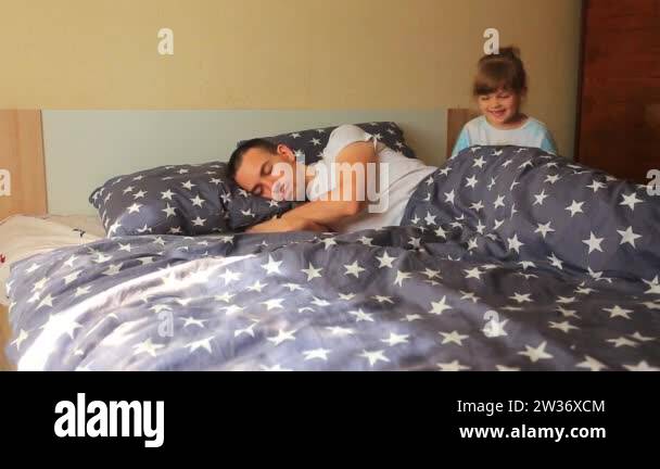 happy little daughter wakes up her sleeping father early in the morning ...