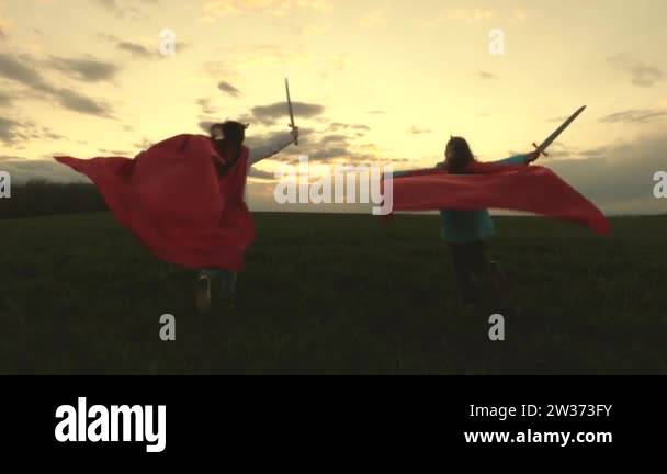 girls in red cloaks run with swords in hand across field playing ...