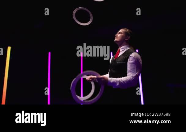 Camera rotates around professional male juggler juggling white rings ...