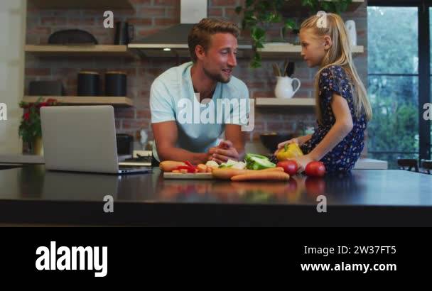 Caucasian girl enjoying her time at home, sitting with her father in the kitchen, using a laptop ...