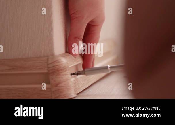 Human hand touches the plastic baseboard with a screwdriver and dowel ...
