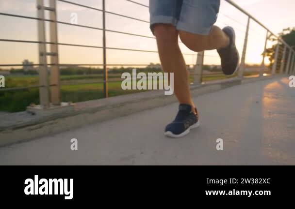 LOW ANGLE: Unrecognizable young man jogs across asphalt bridge at ...