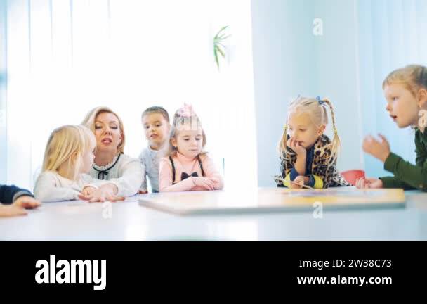 Children with their teacher together at round table in class. Little ...