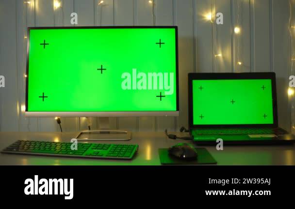 Green screen laptop and pc monitor on a homework desk in dark room with ...