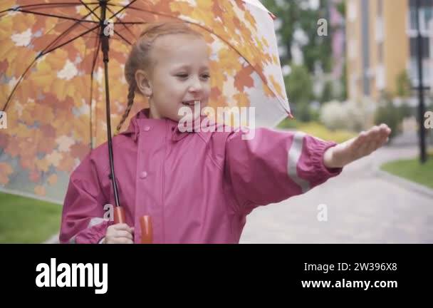 Pretty blond little girl with umbrella checking rain with palm ...
