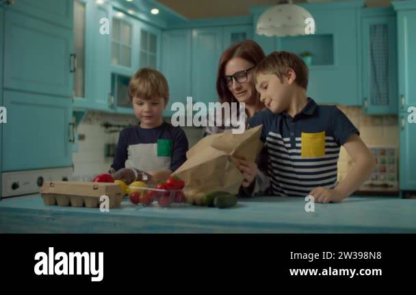 Two kids help young 30s mother to unpack paper bag with fresh food ...
