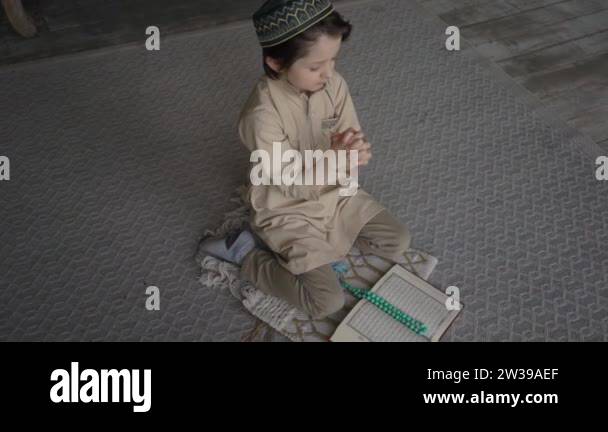 Adorable muslim kid read the Quran in prayer hat and arabic clothes ...