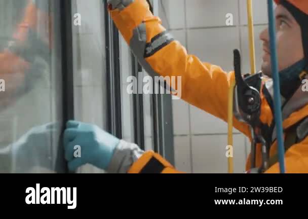 window cleanerin helmet and gloves washes windows with rubber screed ...