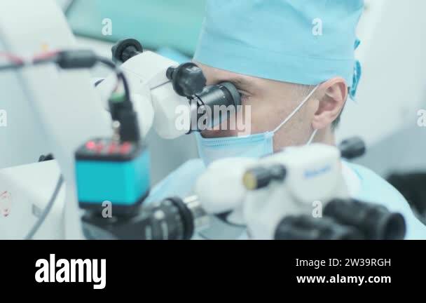 Surgeon looking into the microscope at the eye of female patient at the ...