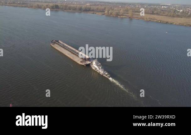 A tugboat ship pushes a barge upstream of the river to transport bulk ...