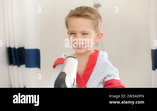 Portrait of cute little boy drying his wet hair with hairdryer after ...