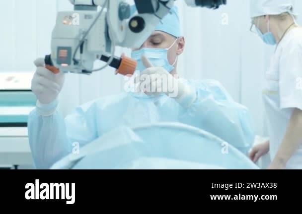 Surgeon looking into the microscope at the eye of female patient at the ...