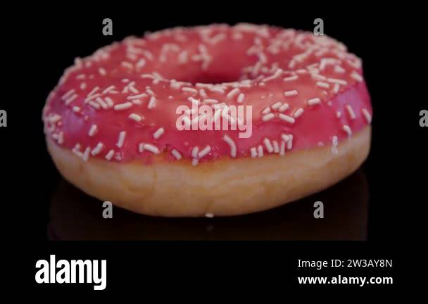 Donut with pink icing and colorful sprinkle rotating on a black ...