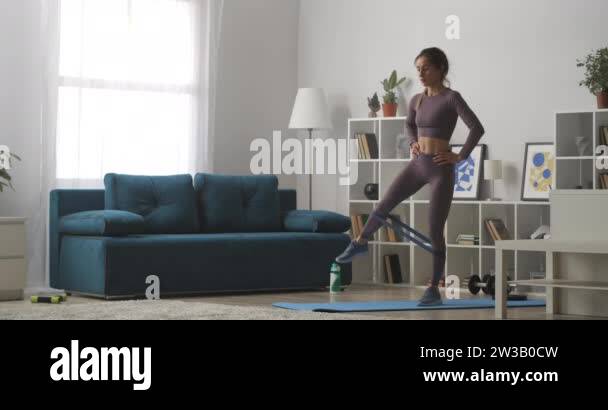 fitness model is training with elastic band on legs, moving leg to side ...