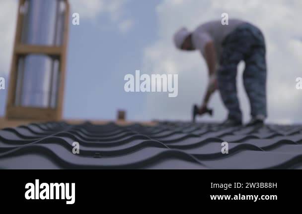Roofing works. The installer screws the metal tile to the roof crate ...