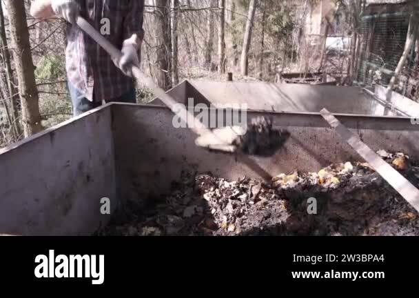 Farmer turning compost heap to aerate and mix up, making organic fertilizer from kitchen and ...