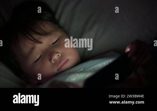 Little girl children playing games at a smart phone at night time light ...