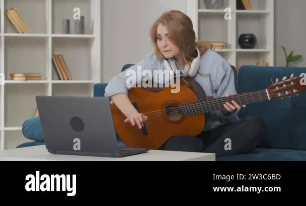 young woman is learning new song on guitar at living room of apartment ...