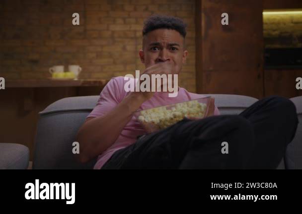 Millennial man watching scary movie eating pop corn sitting alone on ...