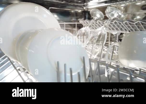 Opening dishwasher unloading dishes. Female hands pull out clean washed ...