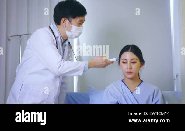 Young male otolaryngologist with stethoscope examining asian female ...