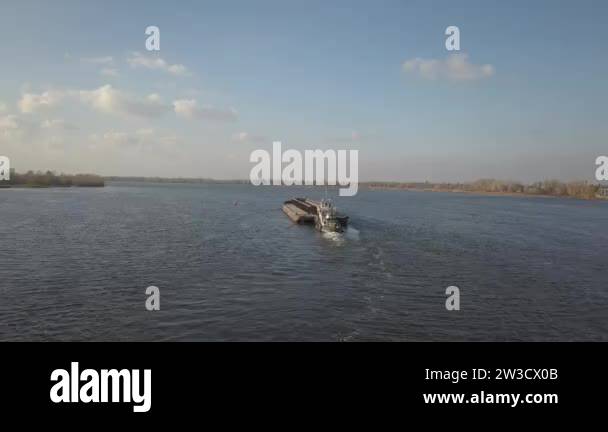 A tugboat ship pushes a barge upstream of the river to transport bulk ...