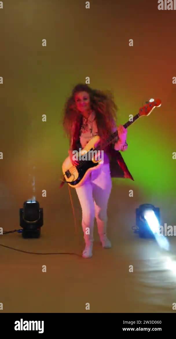 Vertical video of a female bass player in a jacket jumping on one leg ...