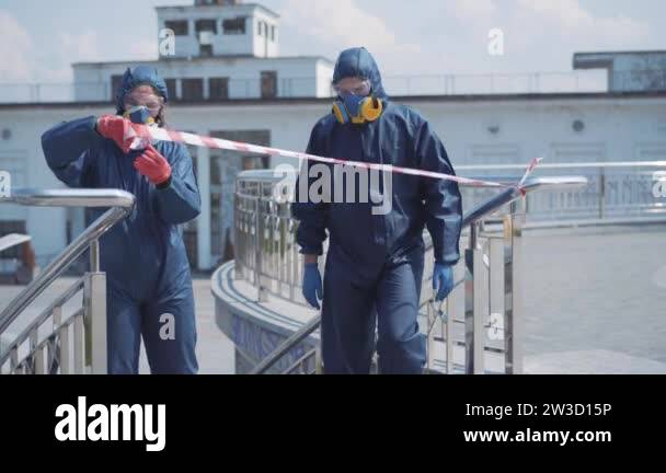 Two Caucasian people in biohazard suits using red and white caution ...
