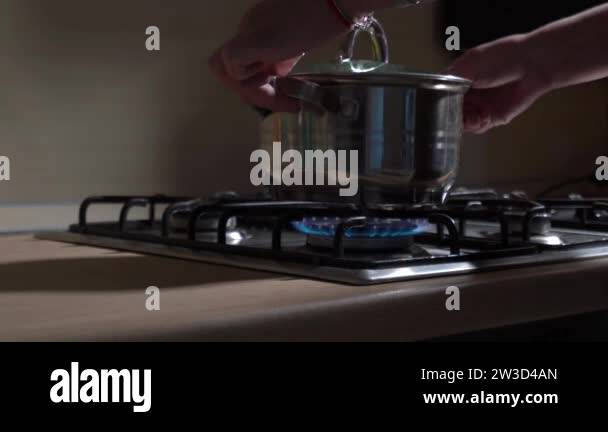 a blue fire burns strongly on a gas stove. female white hands put on a ...