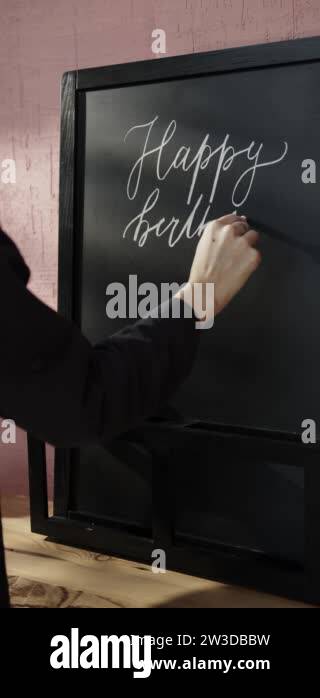writing a birthday greeting in calligraphy on a blackboard using a cha ...