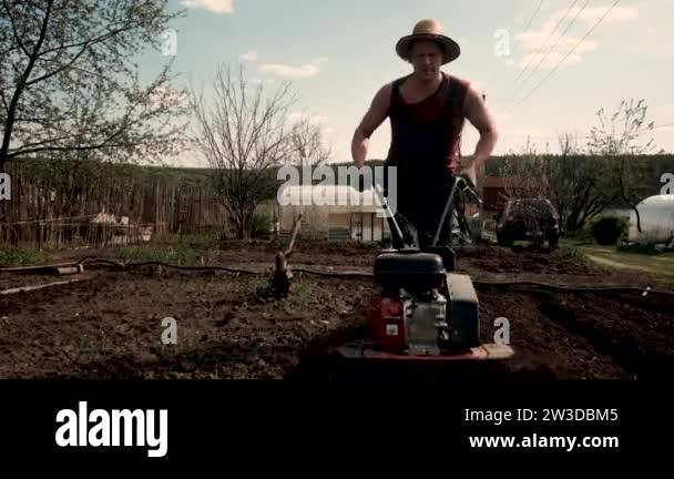young strong man plows on a cultivator in the garden. Soil preparation ...