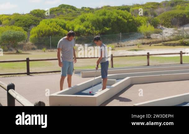 Man with his son playing mini golfers on mini golf course at summer day ...