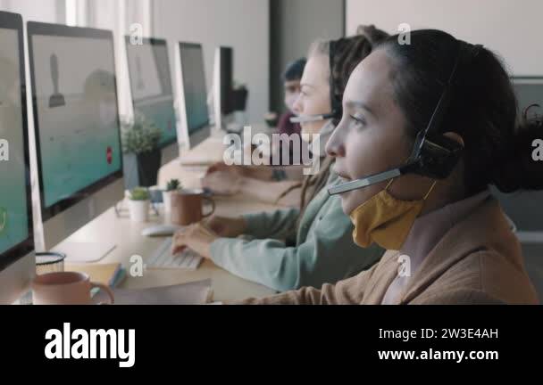 Slowmo side view with PAN of young call center agents in headsets and ...