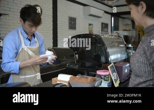 Coffee shop concept. A male employee is ringing a customer. 4k ...