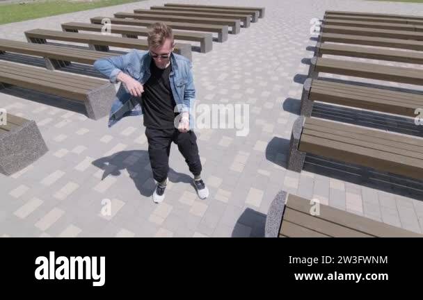 young guy dancing street dance in a park between rows of benches ...