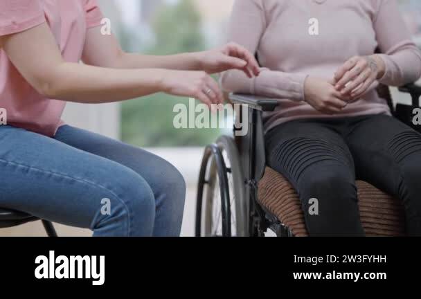Unrecognizable young paralyzed woman and friend holding hands sitting ...