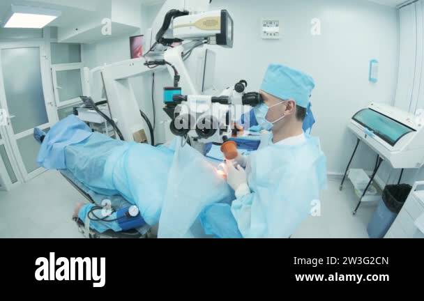 Surgeon looking into the microscope at the eye of female patient at the ...