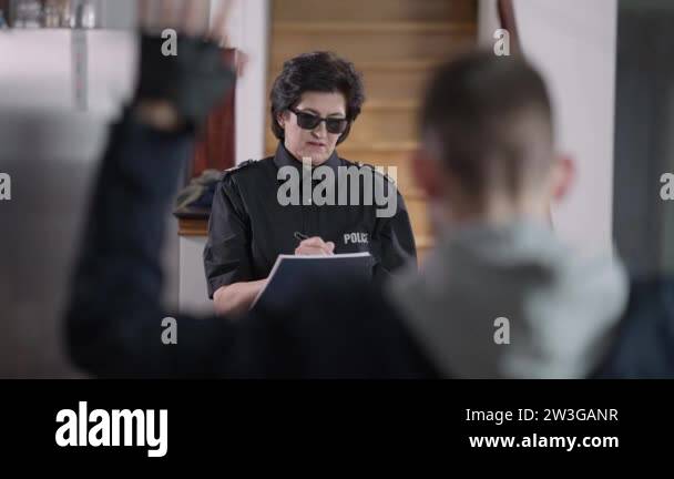 Smiling female police officer in sunglasses talking to blurred arrested ...